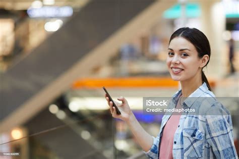 쇼핑몰에 서 있는 파란 셔츠를 입고 카메라를 보면서 소셜 미디어에 메시지를 보내는 예쁜 미소로 양성 아름 다운 소녀 데이트에 대한 스톡 사진 및 기타 이미지 Istock