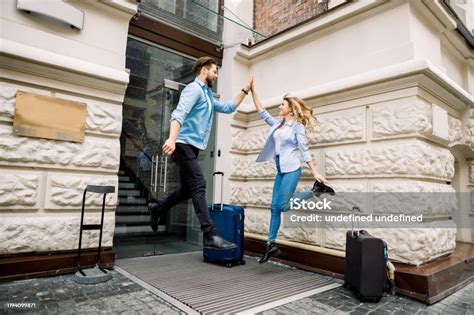 젊은 쾌활한 부부는 호텔에 도착하기 전에 여행 가방 점프와 다섯을주는 재미를 야외에서 즐거운 시간을 보내는 커플 구시 가지 건물 근처 관광객에 대한 스톡 사진 및 기타