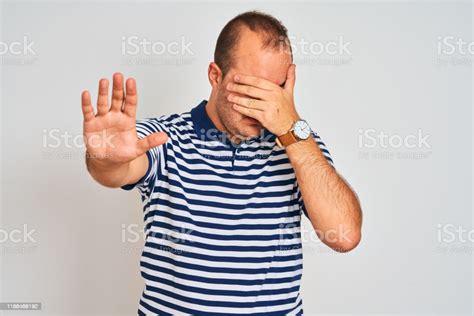 편안한 줄무늬 폴로를 입은 청년은 고립된 흰색 배경 위에 서서 손으로 눈을 가리고 슬프고 두려움의 표정으로 제스처를 멈춥니다 부끄럽고 부정적인 개념 가리기에 대한 스톡 사진