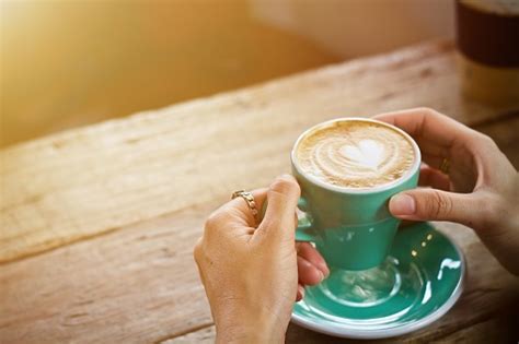 커피 한 잔을 들고 있는 여자의 손을 닫고 아름다운 햇빛을 배경으로 야외 카페에서 커피를 마시며 편안한 시간을 보내고 있다 인생의 단순한 즐거움을 즐기기 0명에 대한 스톡