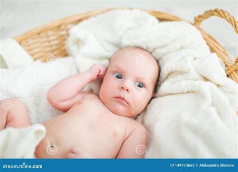 Newborn Naked Baby Is Lying In Wicker Basket Basket On White Wooden