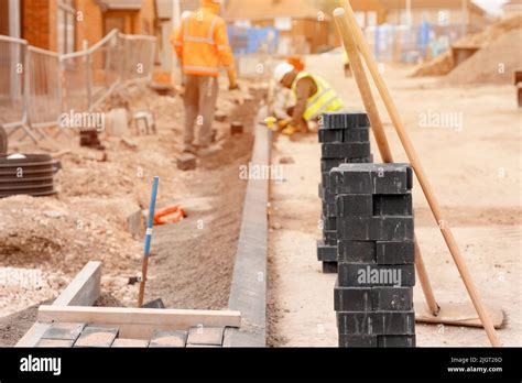 Builders Installing Paving Blocks During Road And Footpath Construction On A Semi Dray Concrete