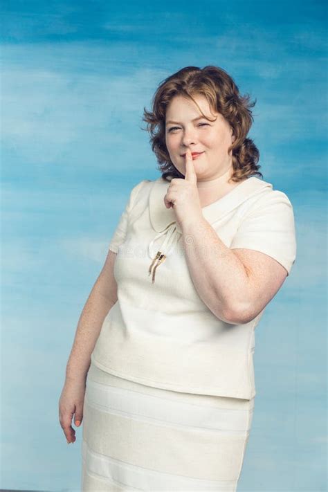A Pretty Chubby Redhead Woman In A White Dress Raised Her Index Finger To Her Lips As A Sign Of