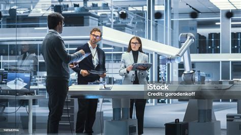 다양한 산업용 로봇 엔지니어 팀이 로봇 팔이 있는 테이블 주위에 모였습니다 과학자들은 태블릿 컴퓨터를 사용하여 로봇을 조작하고 프로그래밍하여 금속 부품을 집어 들고