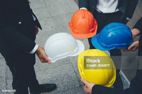 사업가와 엔지니어가 빨간색 흰색 노란색 및 파란색 하드 안전 헬멧을 들고 유니티 및 팀워크 개념 공장 산업 건물에 대한 스톡 사진 및 기타 이미지 Istock