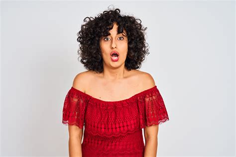 고립 된 흰색 배경 에 서 빨간 드레스를 입고 곱슬 머리를 가진 젊은 아랍 여성은 두려워하고 깜짝 표정 두려움과 흥분 얼굴로 충격 감정에 대한 스톡 사진 및 기타 이미지