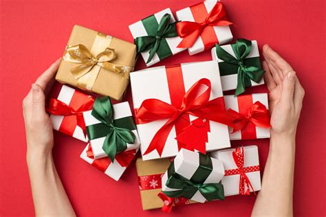 고립 된 빨간 배경에 리본 리본이달린 선물 상자의 더미를 껴안고있는 여성의 손의 1 인칭 탑 뷰 사진 대규모 개체 그룹에 대한