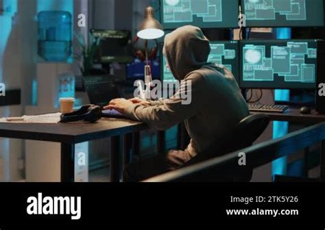 Impostor With Mask Hacking Computer Server Late At Night Working On Laptop And Multiple