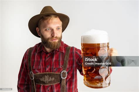 모자를 쓴 수염을 기른 남자의 반길이 초상화와 거대한 머그잔을 들고 있는 바이에른 전통 의상 흰색 배경 위에 고립된 가벼운 거품이 많은 맥주 한 잔 전단 10월에 대한 스톡