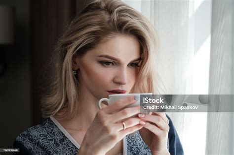 창에 의해 파란색 가운에 아름 다운 젊은 금발 여자 접시와 함께 화이트 컵에서 커피 또는 차를 마신다 아침 햇살 침실 창 가정 생활에 대한 스톡 사진 및 기타 이미지