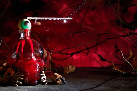 할로윈 피 묻은 칵테일 마가리타 피 묻은 빨간 칵테일 마가리타와 병은 무서운 붉은 어두운 배경에 두개골을 형성합니다 사탕 눈 박쥐 거미와 파티를위한 축제 음료 Dia De