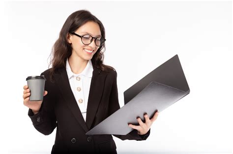 아침에 커피를 마시는 사업가는 상쾌하고 활동적인 아름다운 젊은 일하는 여성이 종이 커피 컵과 폴더를 들고 있습니다 그녀는 안경을 쓰고 흰색 배경에 고립 된 정장을 입고