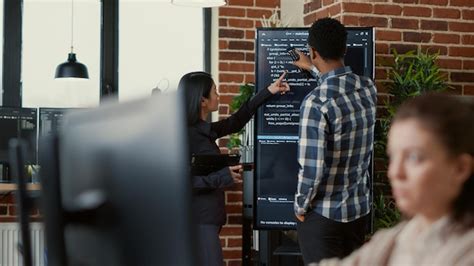 Premium Photo System Developers Analyzing Code On Wall Screen Tv Looking For Errors Comparing