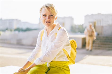 도시 환경에서 여가 시간을 즐기는 세련 된 노란색 배낭 밝은 금발 Hipster 여자의 반 길이 초상화 카메라를 보면 도심에서 야외에서 앉아 긍정적인 젊은 여자 노랑에 대한