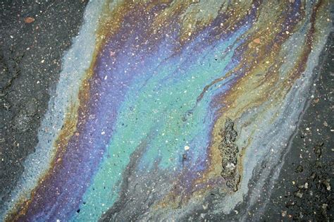 An Oil Slick Spreads Across Asphalt Displaying Vibrant Colors Including Blue And Purple Stock