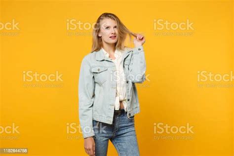 데님 캐주얼 옷에 잠겨있는 아름 다운 젊은 여자의 초상화는 스튜디오에서 밝은 노란색 오렌지 벽 배경에 고립 된 머리를 찾고 들고