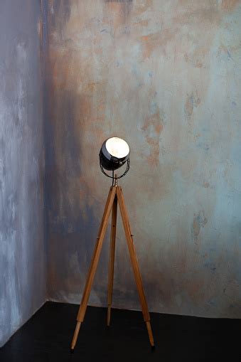 객실 내 삼각대에 세련된 램프 삼각대 빛 프로젝터 장식용 라이트 프로젝터는 회색 콘크리트 벽에 서 있습니다 로프트 거실 인테리어 나무 삼각대에 바닥 램프 로프트 스타일
