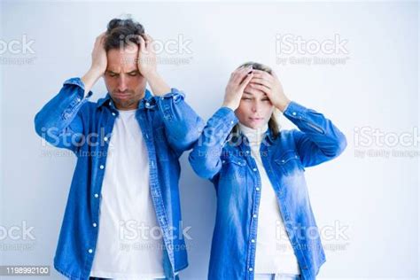 젊은 아름 다운 부부는 고립 된 흰색 배경 위에 서 서 있는 젊은 아름 다운 부부는 두통이 절실하 고 스트레스 때문에 통증과 편두통 머리에 손을 남자에 대한 스톡 사진 및