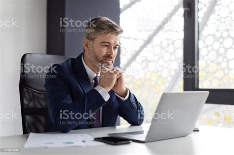 Бизнесмен Средних Лет Сидит За Столом В Офисе Смотрит На Экран Ноутбука — стоковые фотографии и