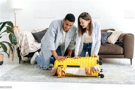 행복한 배우자는 여행을 위해 여행 가방을 포장합니다 백인 젊은 여성과 스페인 남자는 노란색 큰 여행 가방에 물건을 넣고 휴가를 준비하고 거실에서 물건의 전체 여행 가방을