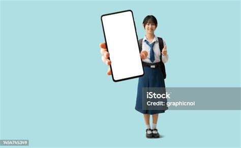 전신 아시아 학생 소녀는 큰 스마트 폰을 들고 손으로 유니폼을 입고 디자인 작업을 위한 클리핑 경로가 있는 파란색 배경에 격리되어 있습니다 빈 여유 공간 14 15 살에