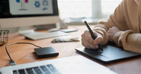 컴퓨터 화면에 클라이언트 중 한 명을 위해 로고를 그리는 동안 터치패드와 스타일러스를 사용하는 젊은 창조적인 남성 프리랜서