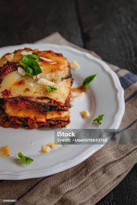 Tradicional 파르미지아나 디 멜란잔 구운 가지 이탈리아 시칠리아 사촌 흰 접시에 치즈 토마토 향신료를 곁들인 구운 가지 나무 탁자 위에 가지 요리가 있습니다