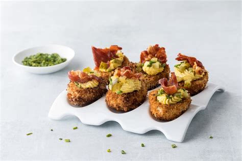 A White Platter Of Deep Fried Deviled Eggs Garnished With Chives And Prosciutto Stock Image