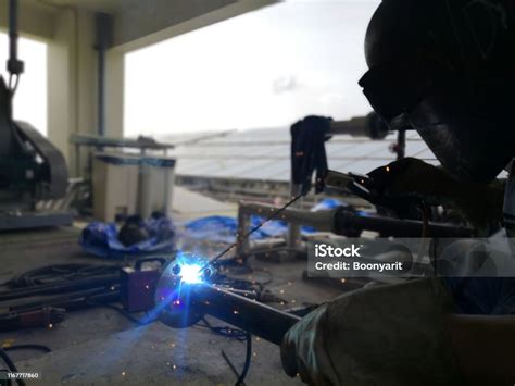 건설 노동자는 용접 마스크와 용접기 가죽을 착용 용접기입니다 검은 강관은 건설 현장에서 용접 기계로 용접 파란색 불꽃은 측면에 날아 강철에 대한 스톡 사진 및 기타 이미지