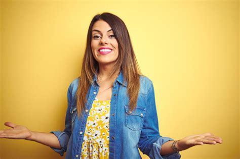 노란 고립 된 배경 위에 서있는 젊은 아름다운 여성은 친절한 환영 긍정적이고 자신감있는 인사로 두 팔을 벌려 쾌활하게 미소 지었습니다 가득 찬에 대한 스톡 사진 및 기타