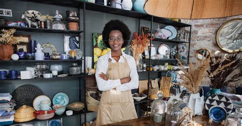 제복을 입고 안경을 쓰고 웃으며 카메라를 바라보는 호감 가는 아프리카계 미국인 여성의 초상화 선반에 다양한 장식이있는 현대적인 상점 사진 Unsplash의 미소 이미지