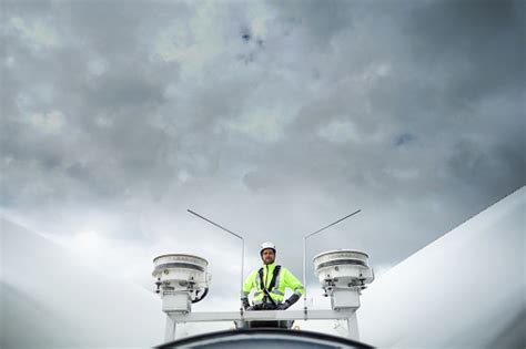 블레이드와 안테나 사이에 풍력 터빈의 지붕 에 서서 카메라를 찾고 전문 로프 액세스 기술자 뒤에 극적인 하늘 엉덩이에 손 해양