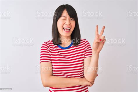 고립 된 흰색 배경 위에 빨간 줄무늬 티셔츠를 입은 젊은 아름다운 중국 여성은 손가락으로 승리 표지판을하고있는 카메라에서 행복한 얼굴 윙크와 미소 2번 T 셔츠에 대한 스톡