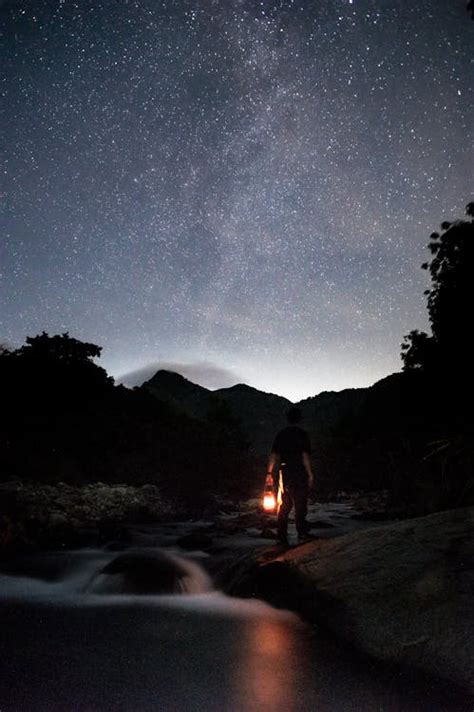 강 검은 하늘 경치가 좋은 고독 고요한 고요함 광야 그림자 긴 노출 남자 등불 락 랜턴 레저 먼 산들 모험 바위 같은 지형 밤 밤 사진 별