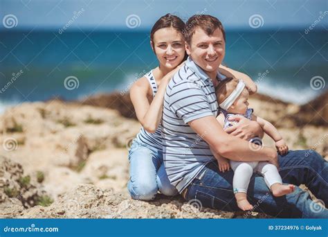 Портрет семьи из трех человек имея потеху совместно берегом океана и наслаждаясь взглядом На