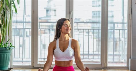 요가를 연습하는 젊은 매력적인 웃는 여자 하프 로터스 운동에 앉아 Ardha Padmasana 포즈 운동 운동복 착용 명상 세션 실내 전체 길이 홈 인테리어