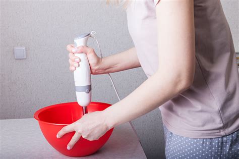 부엌에서 여자는 손에 잠수정 전기 믹서기를 들고 빨간 그릇에 파네톤 반죽재료를 혼합합니다 아내와 어머니의 일상은 가족을 위해 요리하고 있습니다 가정 주방에 대한 스톡 사진
