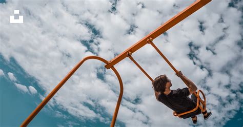 검은 재킷과 파란색 데님 청바지를 입은 남자는 파란색 아래 주황색 금속 바에 앉아 사진 Unsplash의 무료 사람의 이미지
