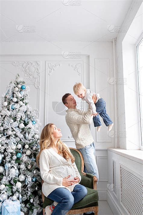 幸福的家庭在家里玩得开心圣诞节的早晨在明亮的客厅里年轻的父母和年幼的儿子父亲怀孕的母亲和他