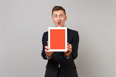 클래식 블랙에 놀란된 젊은 사업가 셔츠 회색 배경에 고립 된 빈 빈 화면으로 태블릿 Pc 컴퓨터를 들고 벌 성과 경력 부 비즈니스 개념입니다 복사 공간을 비웃는 다 검은색에