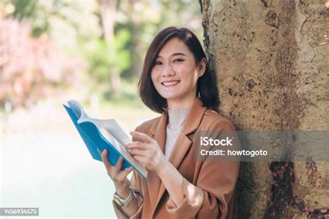 녹색 공원 자연에서 야외에서 책을 읽는 행복한 아시아 여성 독서 책 잡지 휴식 여자 녹색 공원에 앉아있는 레저 초상화 여성 미소 행복한 얼굴로 전자 책 일기 플래너를