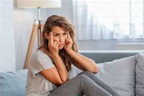 두통으로 집에서 소파에 앉아 고통을 느끼고 몸이 좋지 않은 표정으로 매력적인 여성의 초상화 사진 Unsplash의 좌절 이미지