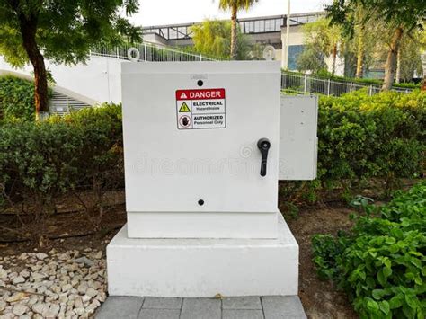 White Outdoor Electrical Box With Warning Label Placed In Landscaped