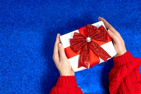 파란색 반짝이 배경 위에 빨간 리본이있는 상자상자를 들고있는 빨간 스웨터를 입은 소녀의 손 2020년에 대한 스톡 사진 및 기타 이미지 Istock