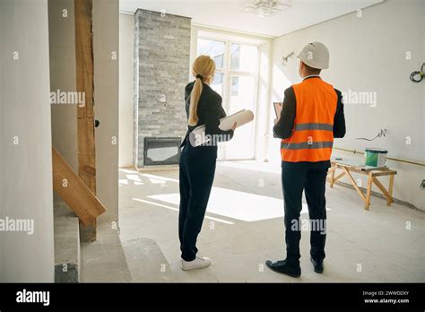 Female Client And Male Engineer Standing In Room Under Construction