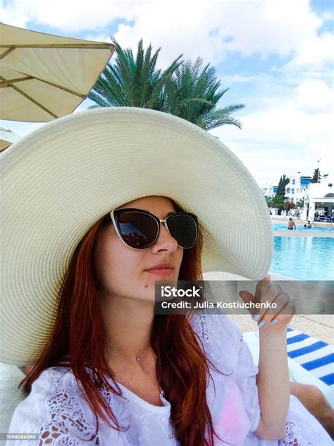 모자를 쓴 매력적인 어린 소녀가 수영장 옆에 앉아 웃고 있다 관광 휴가 및 레크리에이션의 개념 호텔 단지의 광고 간판에 대한 스톡 사진 및 기타 이미지 Istock