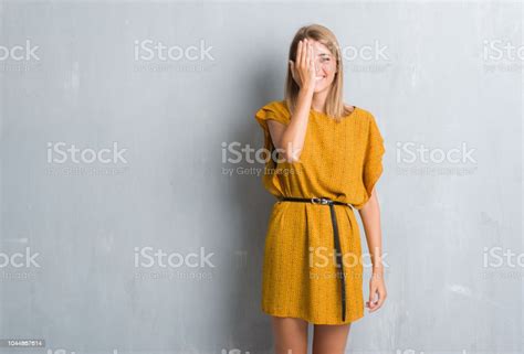 서 그런 지 회색 벽 얼굴과 놀라운 감정에 확신 미소와 함께 손으로 한쪽 눈을 덮고 드레스를 입고 아름 다운 젊은 여자 가리기에 대한 스톡 사진 및 기타 이미지 Istock