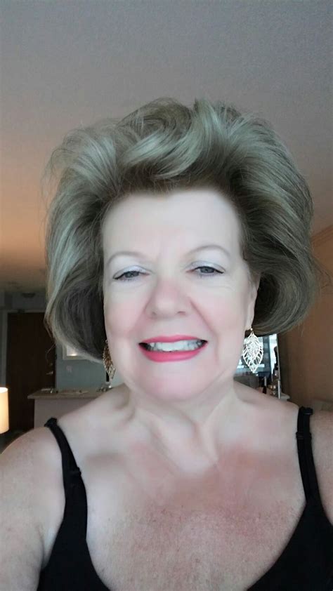 An Older Woman With Gray Hair And Black Top Smiling At The Camera In A Living Room