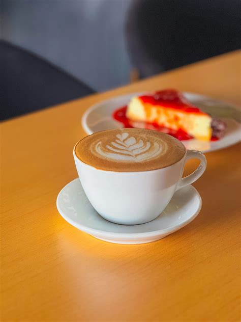 신문이 있는 카페 테이블 위의 카푸치노와 케이크 · 무료 스톡 사진