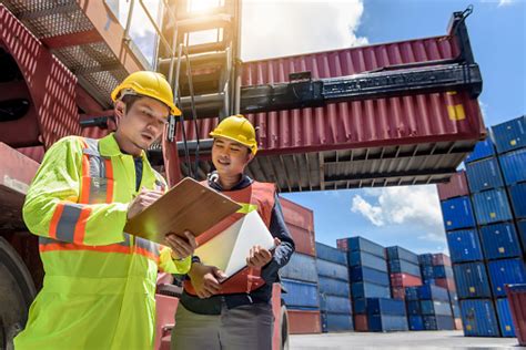 컨테이너 마당의 지게차 화물 근처에 서 있는 노란색 하드햇을 착용한 엔지니어 남성은 화물화물 선에서 화물 컨테이너 박스를 수입 및 수출하는 제어 하중 컨테이너 상자를